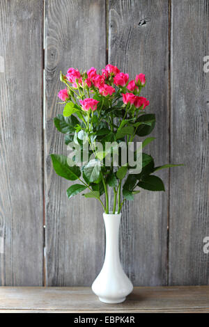 The red roses are in the vase with small plants on the shelf Stock ...