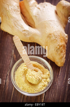 Brown dish with grated ginger, a wooden spoon with powder, ginger root ...