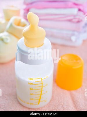 Bottle of milk for baby with pacifier and clothes on table in room ...