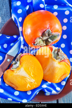 Ripe persimmons on plate, on wooden background Stock Photo - Alamy