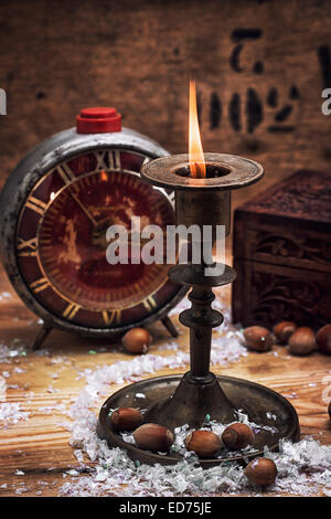 Burning candle in an old brass candlestick and carnival masks on an old ...