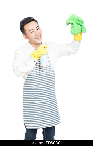 Young man in apron cleaning shelf with pp-duster at home Stock Photo ...