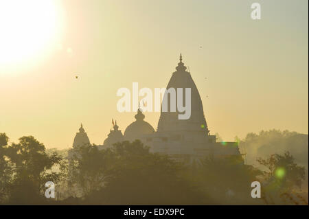 A temple silhouette against a rising sun next to a big pond in kerala ...