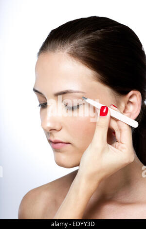 Girl pulling eyebrows with tweezers. Young woman looking at mirror ...