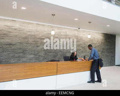 Man standing at reception desk, Talking to Receptionist, side view ...
