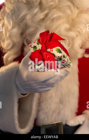 The hand of santa claus holding a gift on red background. The season ...