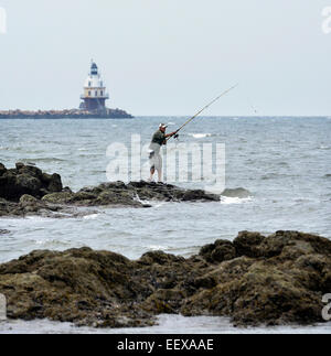 A man casts his fishing line into the sea, with towering skyscrapers on ...