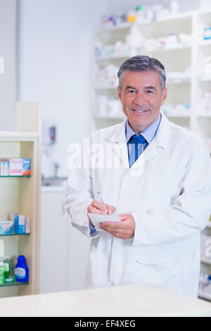 Smiling adult pharmacist writing down assortment of drugs in pharmacy ...
