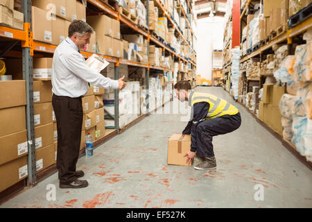Manager watching worker carrying boxes Stock Photo - Alamy