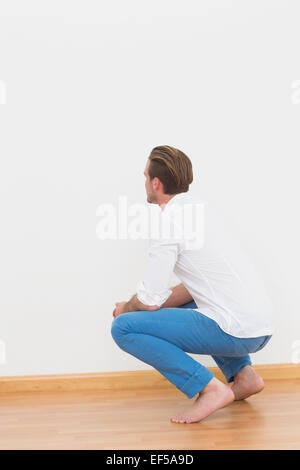 Casual man crouching on floor looking at wall at home Stock Photo - Alamy