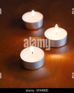 Three white, lit tea candles forming a triangle on an off-white ...