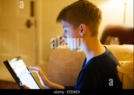 Teen age boy and his iPad, concentrating. A youbger blonde girl is ...