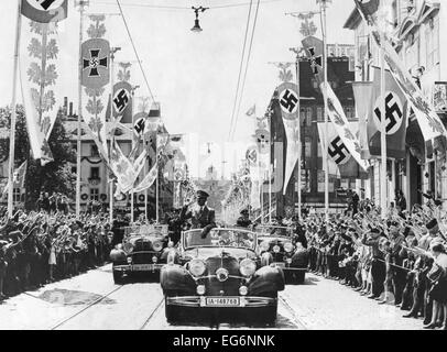 Adolf Hitler waving to crowds from his car at the head of a parade. The ...