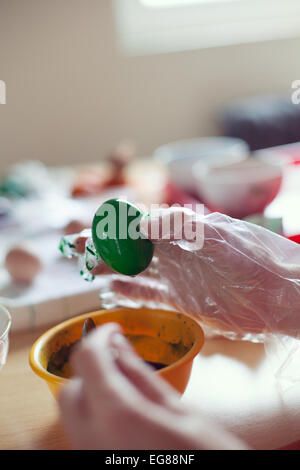 Female hands painting an egg in yellow with a brush on a wooden table ...