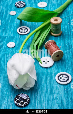 one white tulip and buttons with threads on turquoise wooden background ...