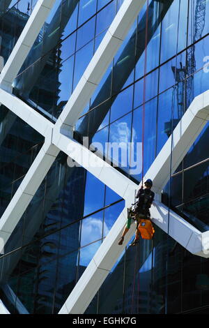 A window cleaner works suspended in a harness along with his tools of ...