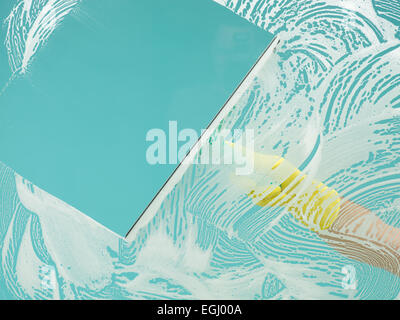 Female hand with squeegee and detergent washing glass against blue ...
