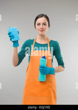 Young woman with cleaning supplies in shopping cart on red background ...