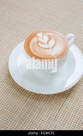 White cappuccino cup with with latte art heart placed on light brown ...