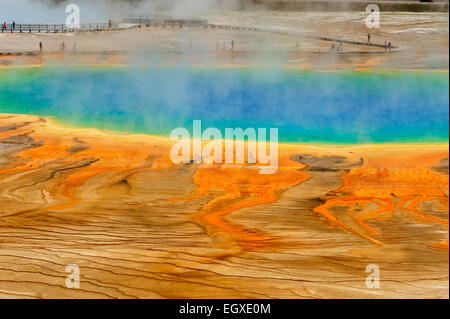 Tourists exploring geyser basin and mountains with cloudy sky in ...
