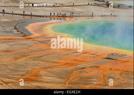 Tourists exploring geyser basin and mountains with cloudy sky in ...