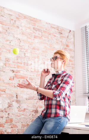 Young woman throwing tennis balll at desk Stock Photo - Alamy
