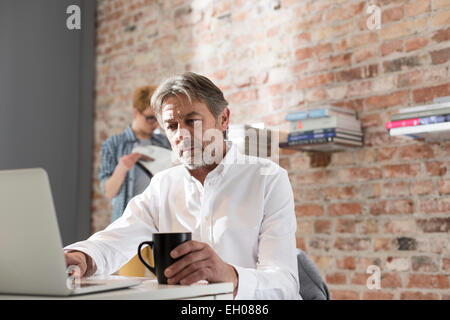Businessman Using Laptop At Desk In Busy Office Stock Photo - Alamy