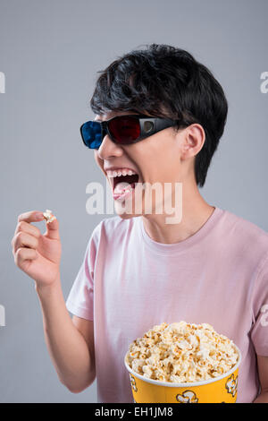 Young man watching a 3d film and eating popcorn Stock Photo - Alamy