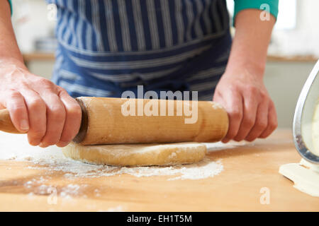 Close-up of female hands rolling dough with pin on wooden table ...