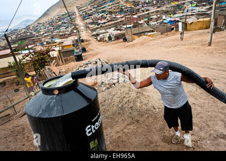 A Peruvian water distribution worker with a pipe fills a plastic barrel ...