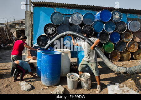 A Peruvian water distribution worker with a pipe fills a plastic barrel ...