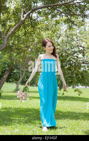 Chinese young woman holding bouquet of white flowers with hand on chin ...