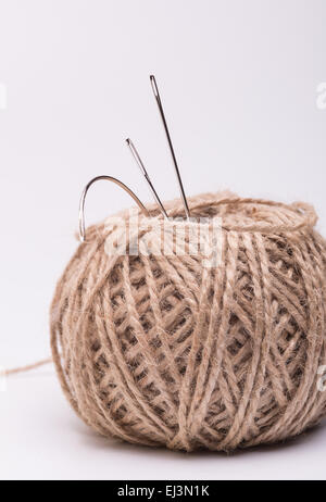 a needle stuck into the brown skein of thread on a white background Stock Photo - Alamy