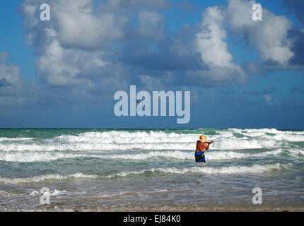 A man casts his fishing line into the sea, with towering skyscrapers on ...