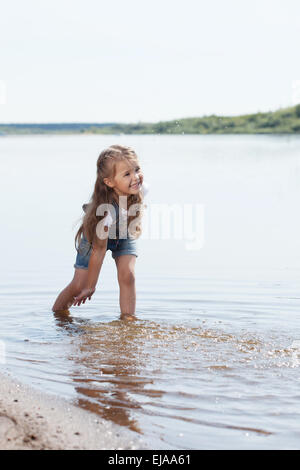 Cute little girl playing by the lake on a windy day, wearing colorful ...