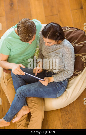young couple cuddling using tablet together while sitting in bean bag ...