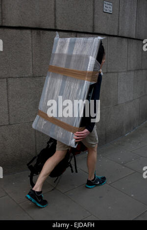 A man carrying a heavy and awkward load on his shoulders through the ...