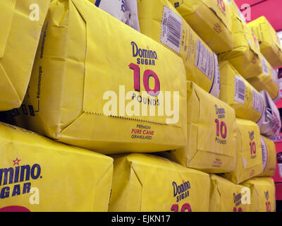 Yellow 10 pound bags of Domino sugar are stacked in a warehouse-style ...