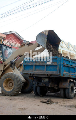 A skip loader is dumping dirt into a dump truck on a city street in ...