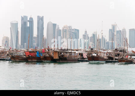 A fleet of dhow boat docked in a port, with the skyline of Doha, Qatar ...