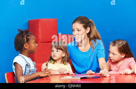 Group of kids talking about book with nursery teacher in preschool ...