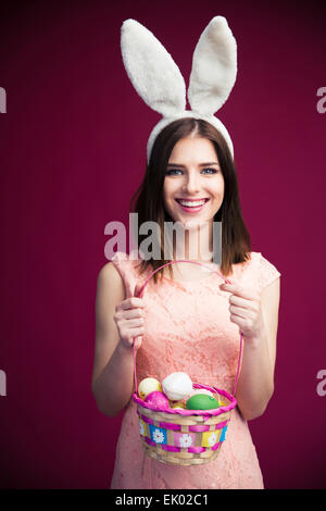 Happy woman in bunny ears with toy carrot on blue background. Easter ...