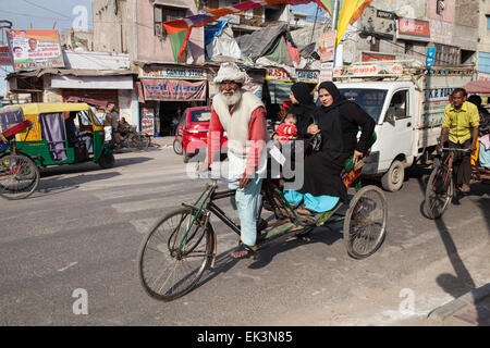 Muslim women travel by rickshaw in crowded street scene in city of ...