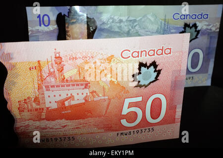A Canadian $50 note next to a $10 note photographed against a black ...