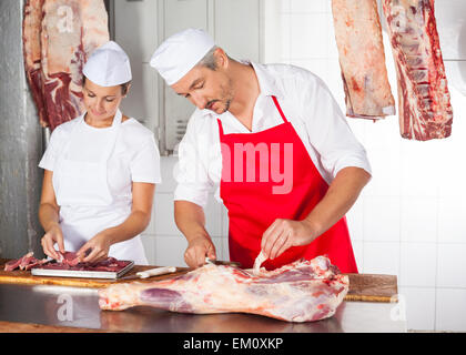 Butcher Cutting Meat By Colleague In Shop Stock Photo - Alamy