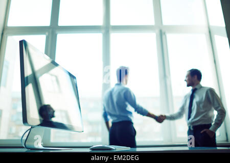 Computer monitor at workplace with two handshaking businessmen on ...