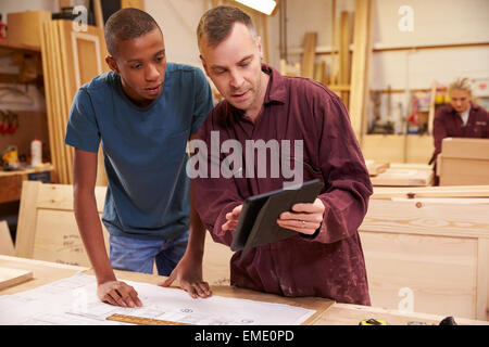 Carpenter With Apprentice Looking At Plans In Workshop Stock Photo - Alamy