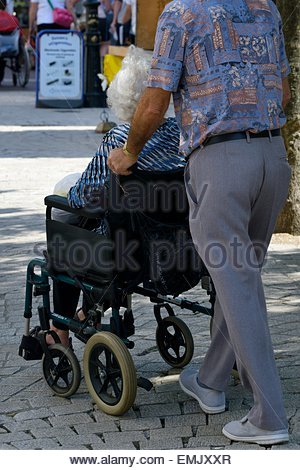 Woman pushing older man in wheelchair up step or ramp onto pavement ...
