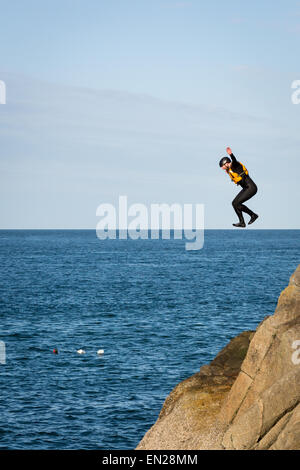 Man in wetsuit, helmet and lifejacket jumping off rocks into sea ...