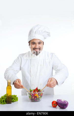 smiling chef holding bowl with vegetables and looking at colleague at ...